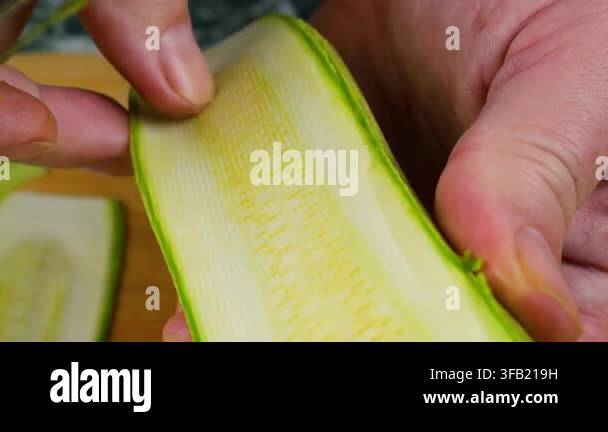 A close-up shot captures a chef using a white vegetable peeler to slice ...