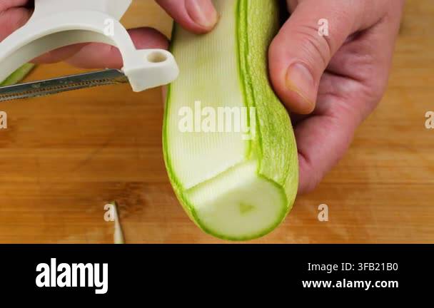 A close-up shot captures a chef using a white vegetable peeler to slice ...