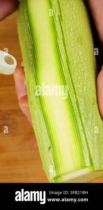 A close-up shot shows a chef using a white vegetable peeler to slice a ...