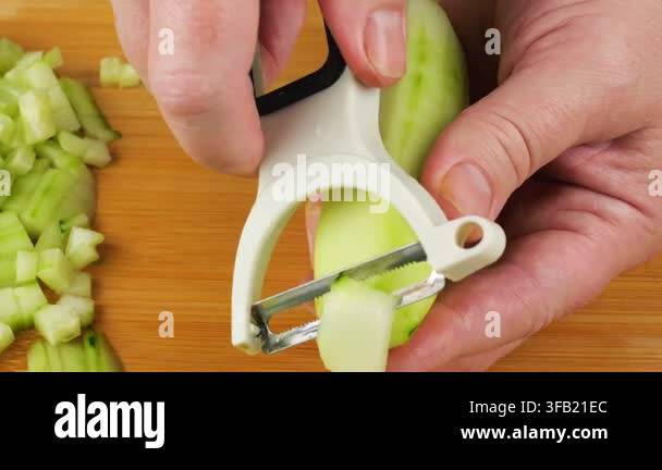 A close-up shot captures a chef using a white vegetable peeler to slice ...