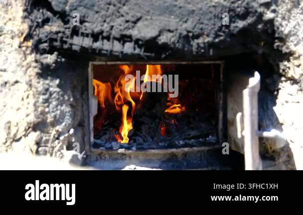 Old rustic homemade metal stove burns with bright wood fire while a ...
