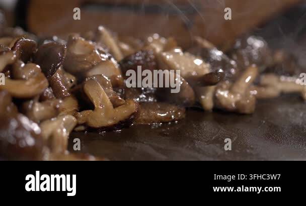 Close view of mushrooms cooking on a frying pan. Smoke rises as they ...