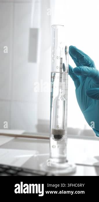 Close-up of a laboratory worker using a hydrometer in a graduated ...