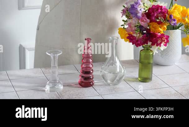 Woman putting beautiful freesia flowers into different vases at tiled ...