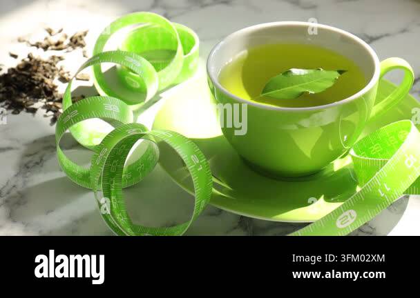 Cup of weight loss tea and measuring tape on white marble table ...