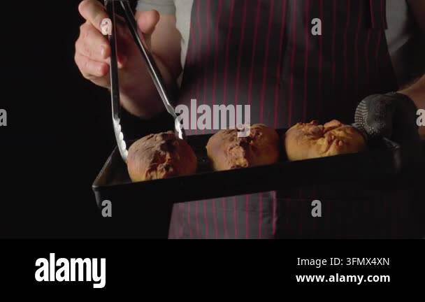 Chef in striped apron holds a tray of freshly baked pastries with tongs ...