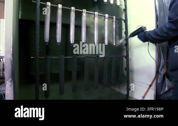 Powder coating operator spraying black paint metal pipes hanging rack ...