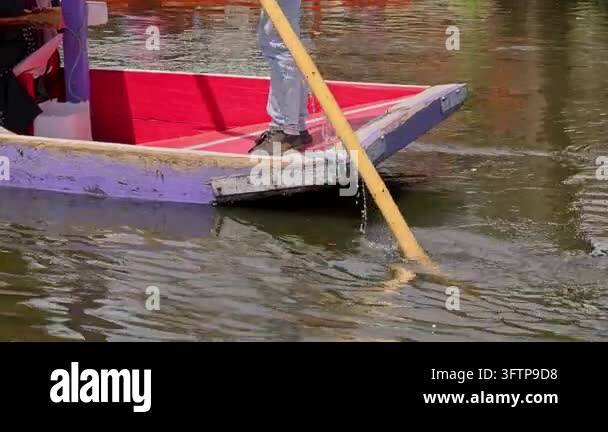 A person uses a wooden oar to propel a vividly painted trajinera boat ...