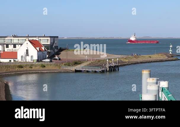 Wide shot of a red cargo ship sailing on the sea past a coastal town ...