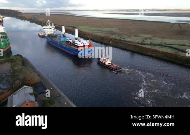 Large cargo ship being assisted by a tugboat in a calm river during the ...