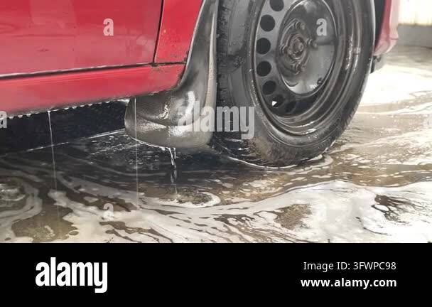 Car wheel beside red vehicle dripping with water after washing process ...