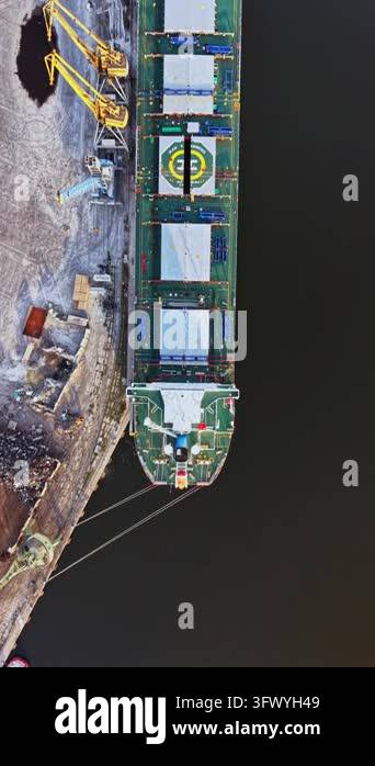 A cargo ship carrying containers is tied to a riverbank at an ...