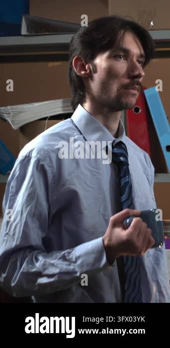 A young businessman in a shirt and tie stands beside shelves filled ...