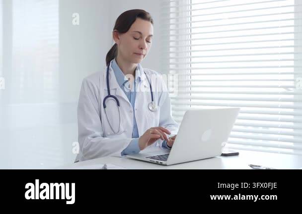 Confident female doctor wearing a lab coat and stethoscope sits at a ...