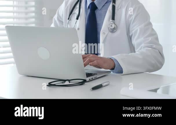 Medical doctor wearing lab coat and stethoscope is sitting at desk and ...