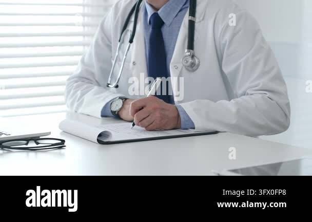 Male physician wearing a lab coat and stethoscope, sitting at a desk in ...