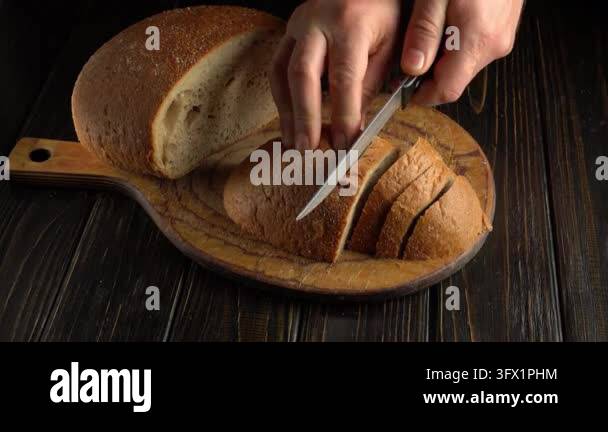 Hands use a sharp bladed knife to slice crusty bread into even pieces ...