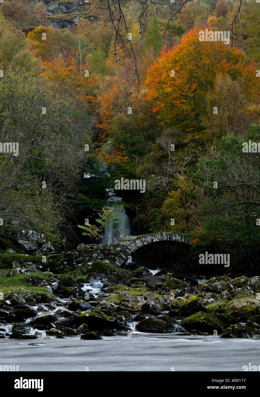 Waterfall surrounded by Autumn leaves with old stone arched bridge and ...