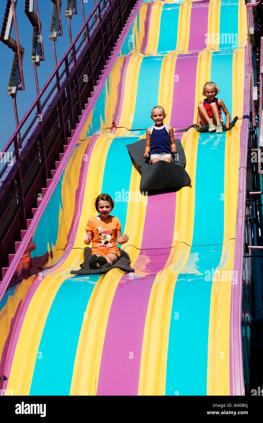 Image of three young girls coming down a colorful slide at a carnival ...