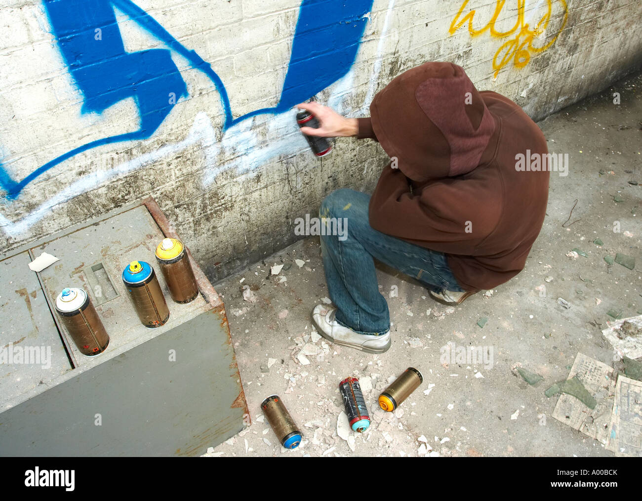 hooded graffiti artist crouching & spraying Stock Photo - Alamy