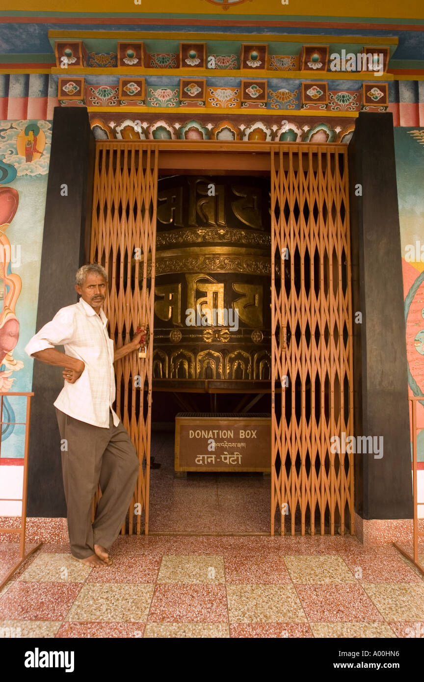 A Indian man standing behind huge golden prayer wheel Tibetan Monastery ...