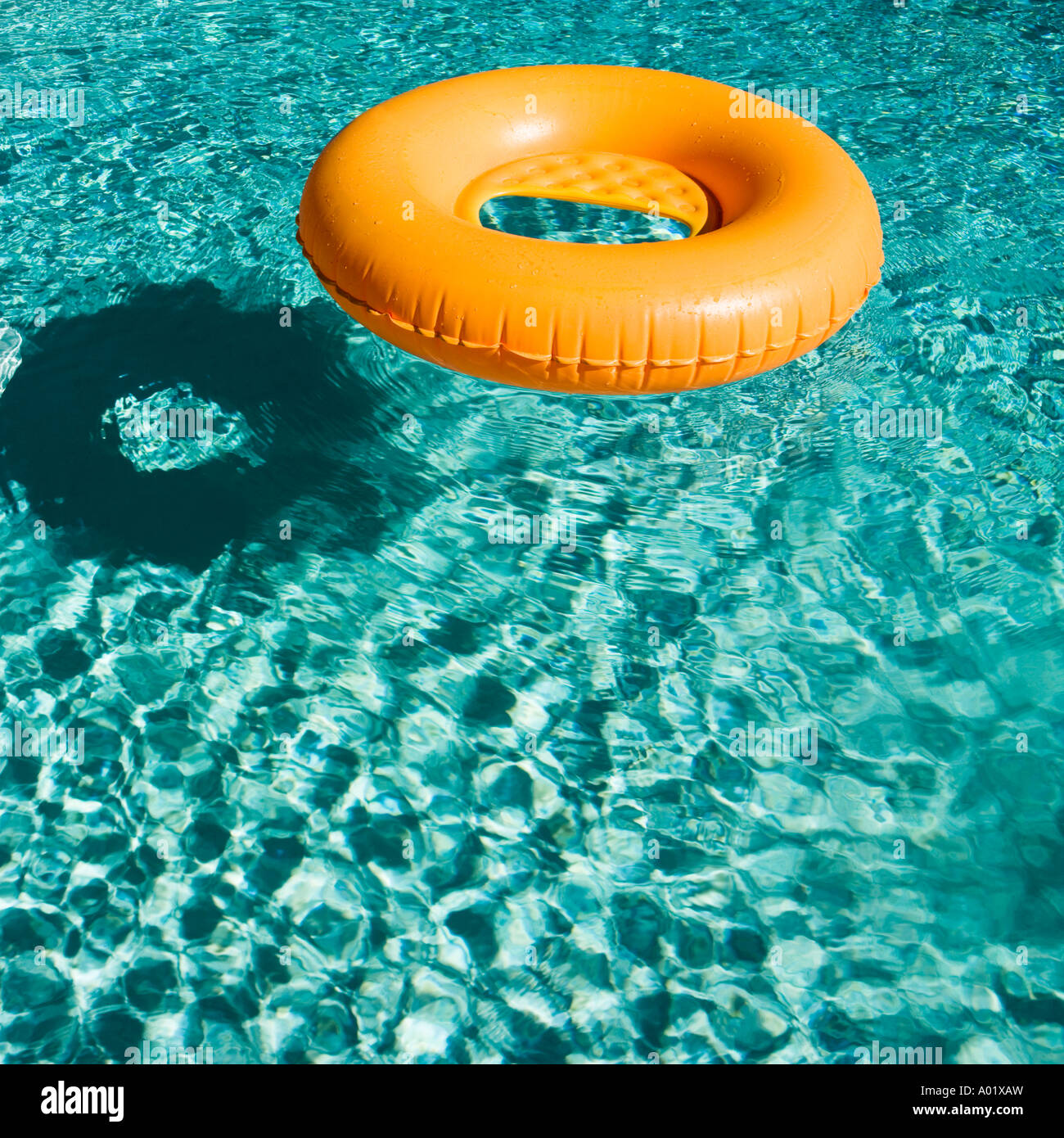 Orange inflatable ring floats in a blue swimming pool casting a shadow ...