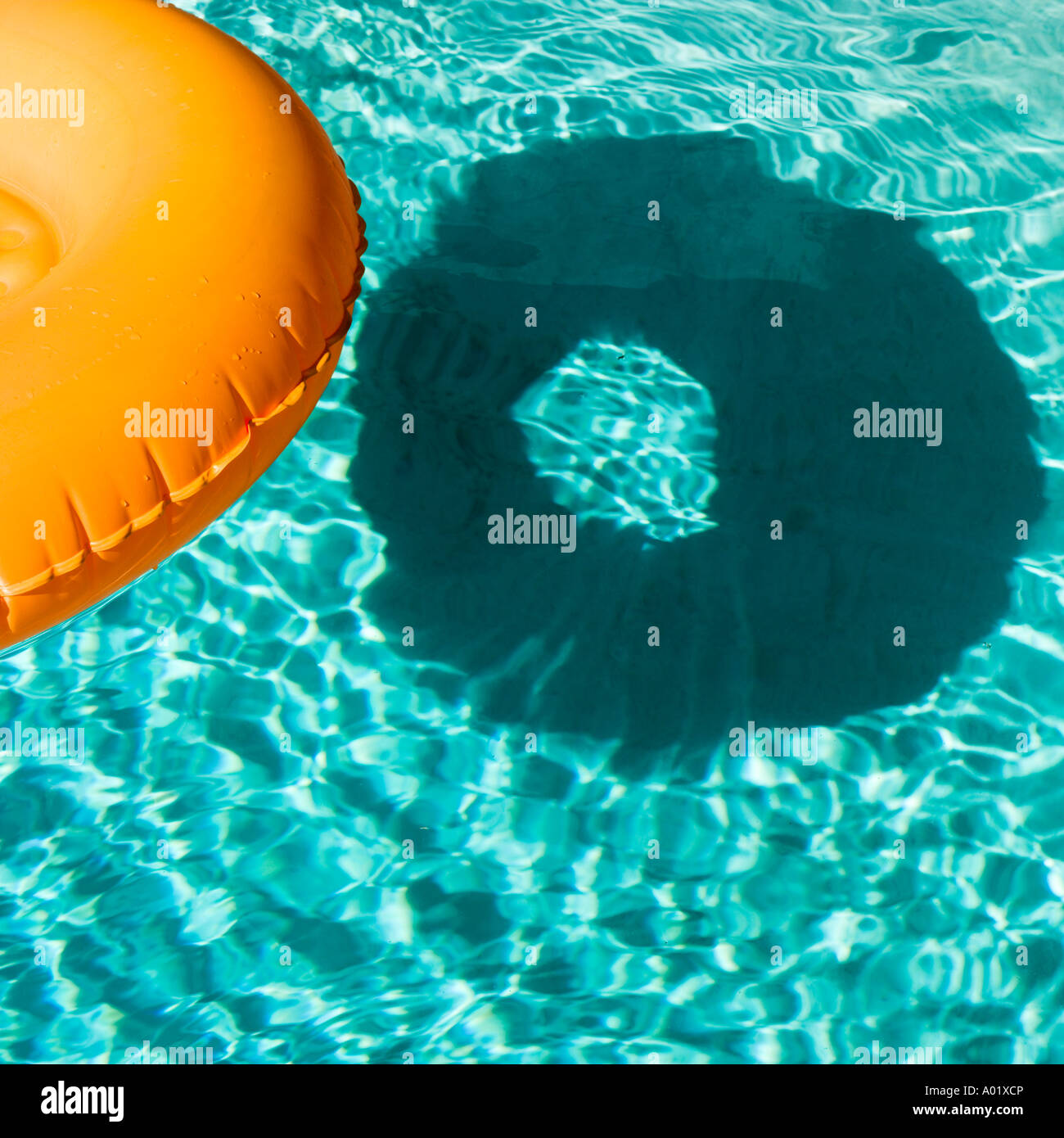 Orange inflatable ring floats in a blue swimming pool casting a shadow ...