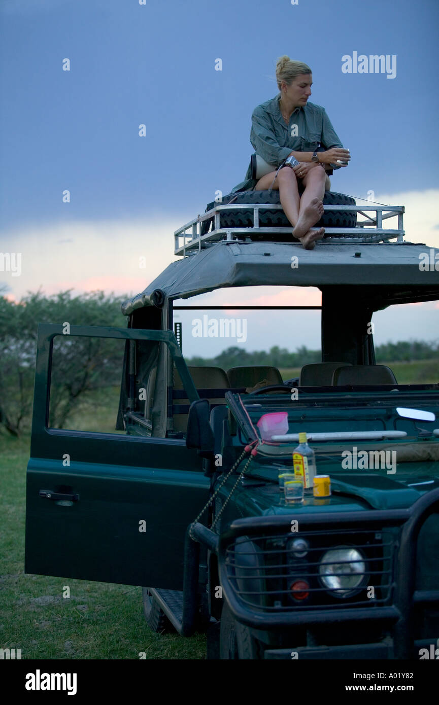 Woman atop safari Land Rover at sunset Moremi Reserve Botswana Africa ...