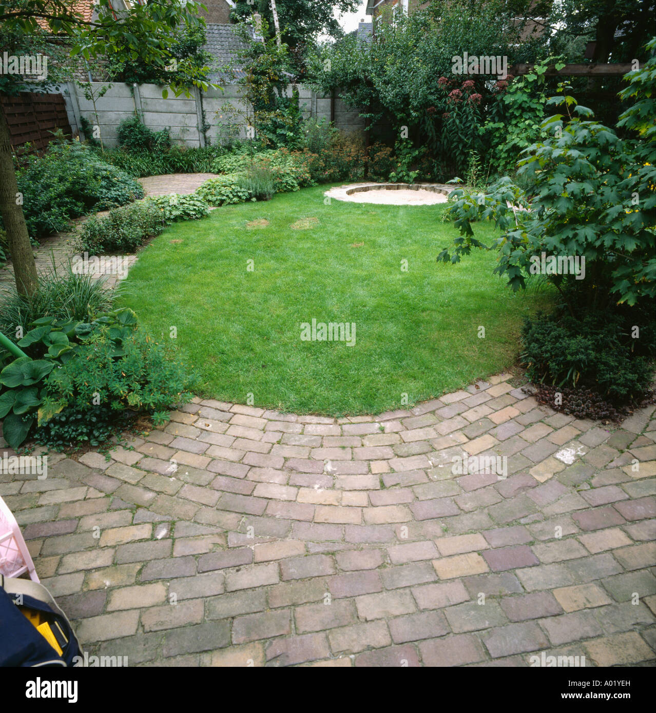 Brick paving around circular lawn in tree-lined town garden Stock Photo ...