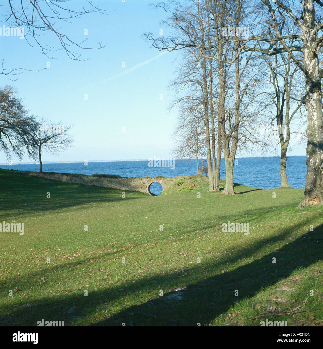 Lawn with trees in front of wall with moongate and view of the ocean ...