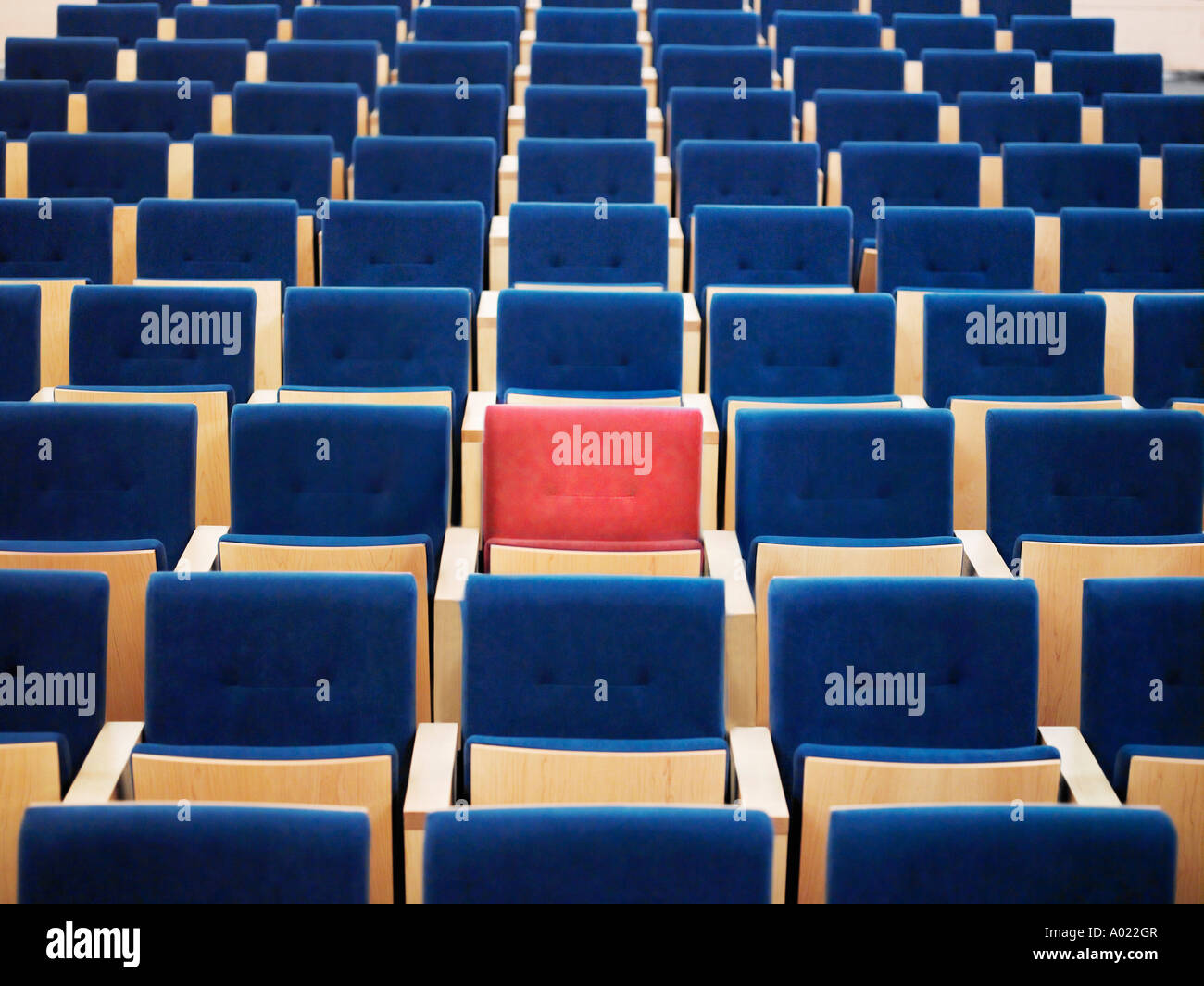 One Red Seat in large group of blue seats in auditorium Stock Photo - Alamy