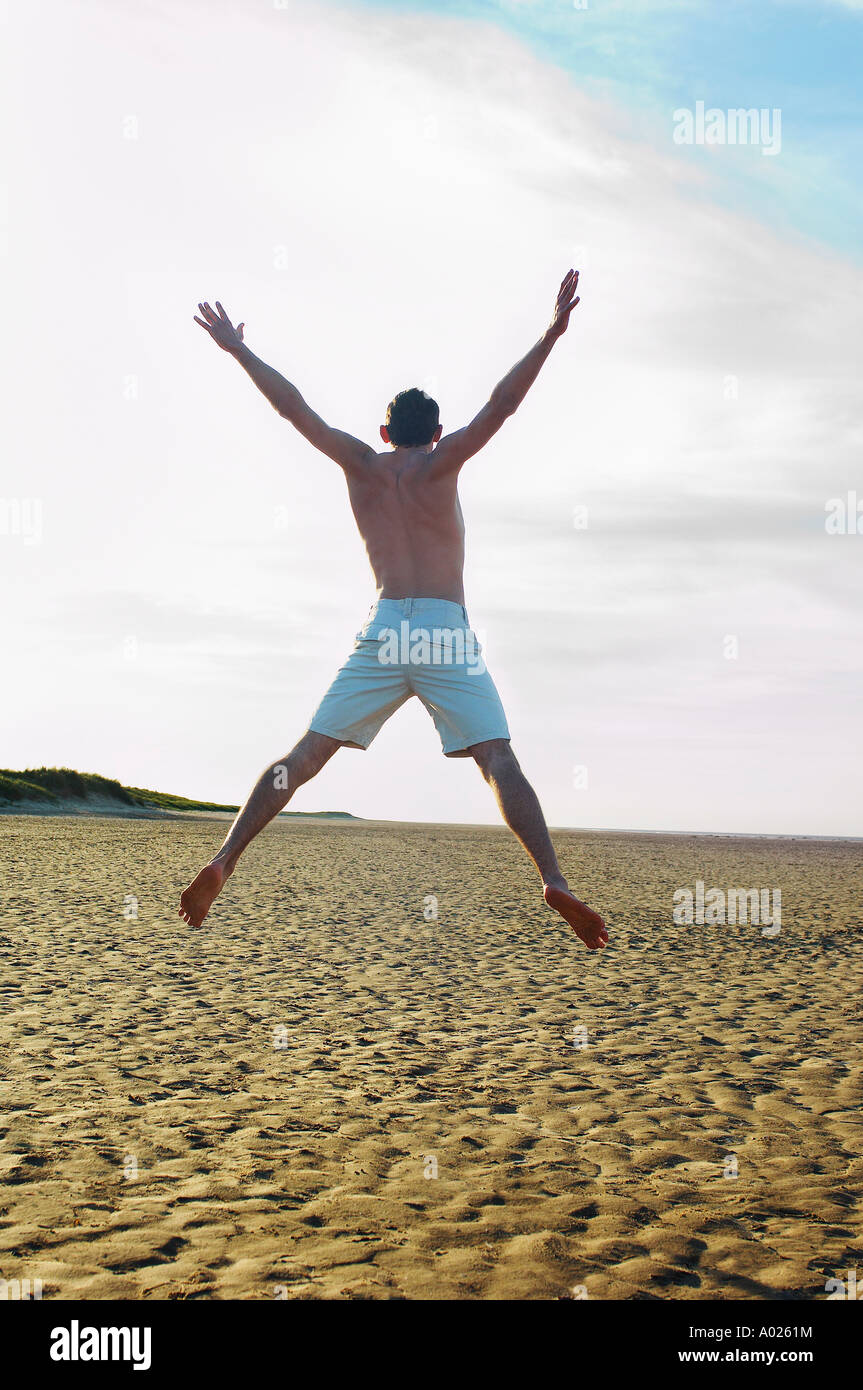 Man on beach doing star jump, back view Stock Photo - Alamy