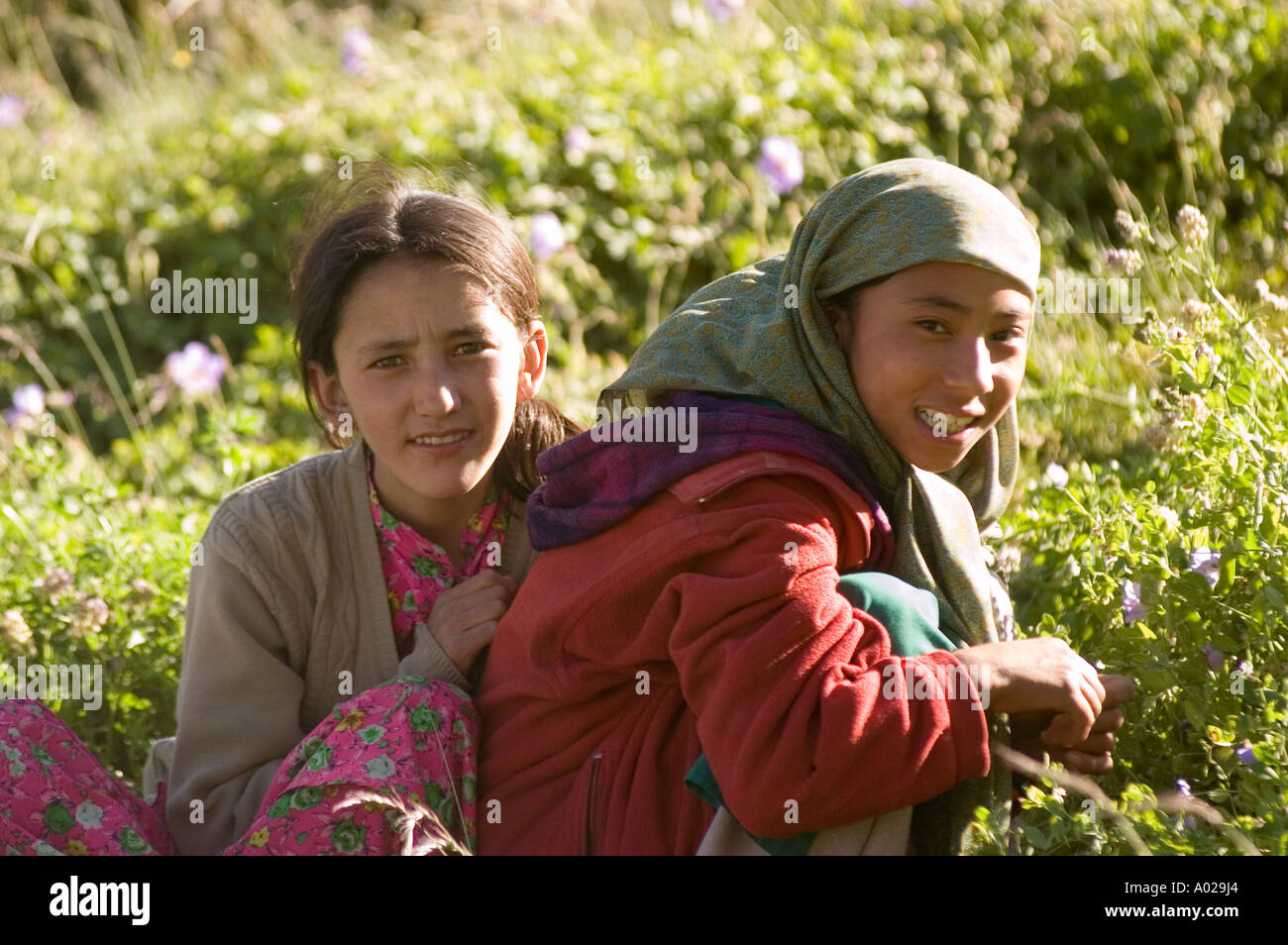 Two young Ladakhi girls in traditional dress looking at camera and ...