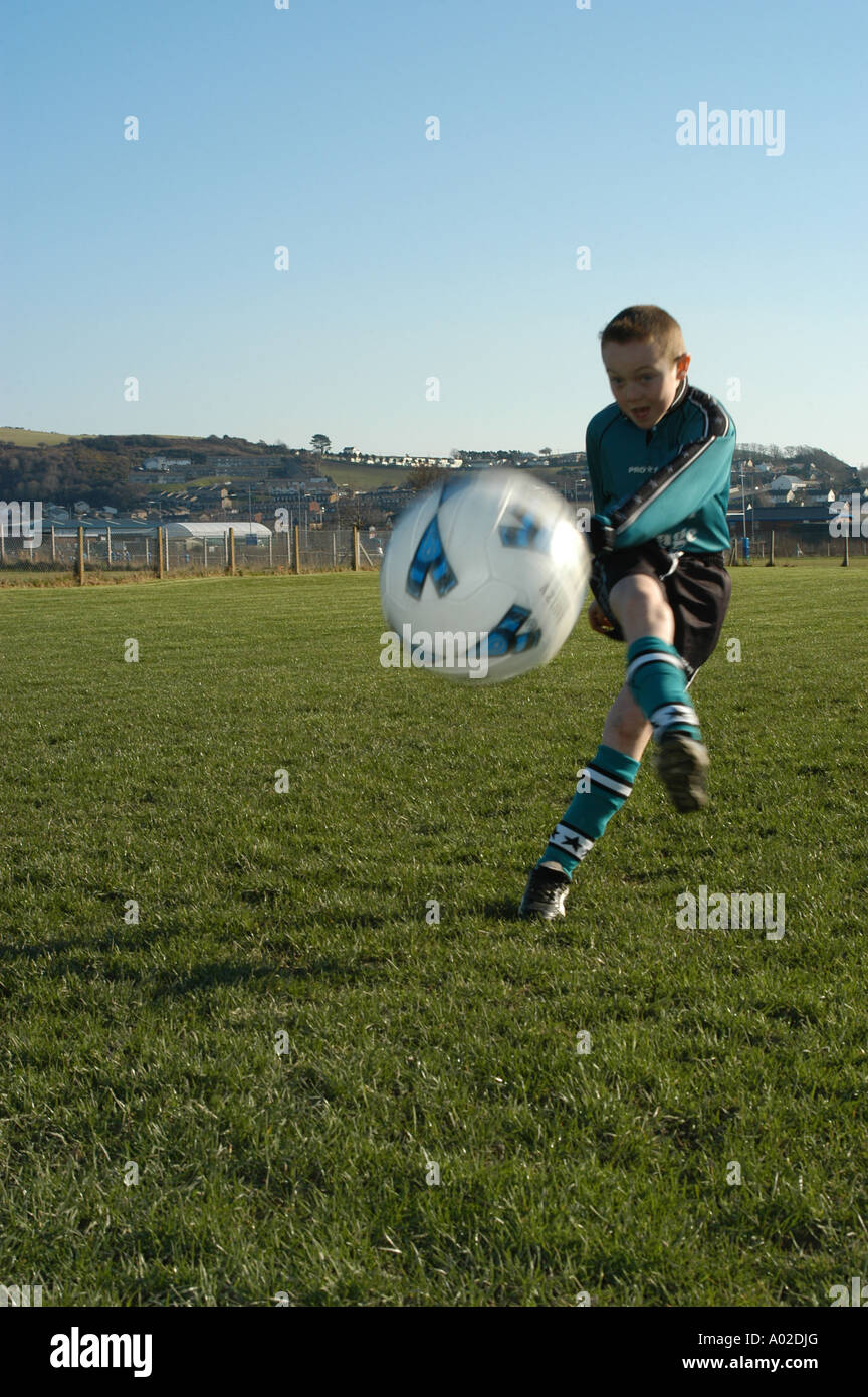 A young boy kicking football straight at the viewer, soccer sport game ...