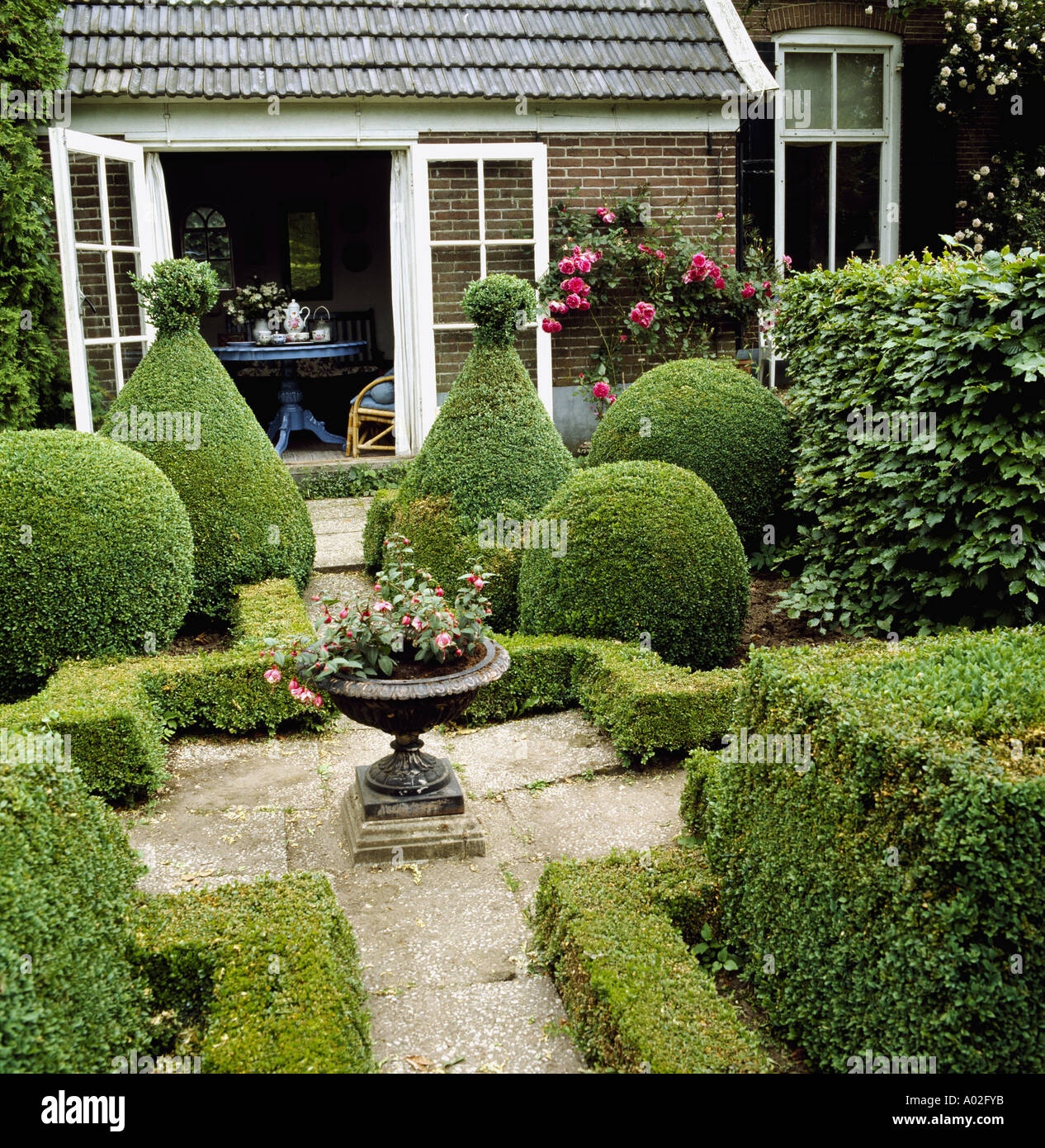 Small courtyard by open french windows with a fuchsia in a stone urn ...