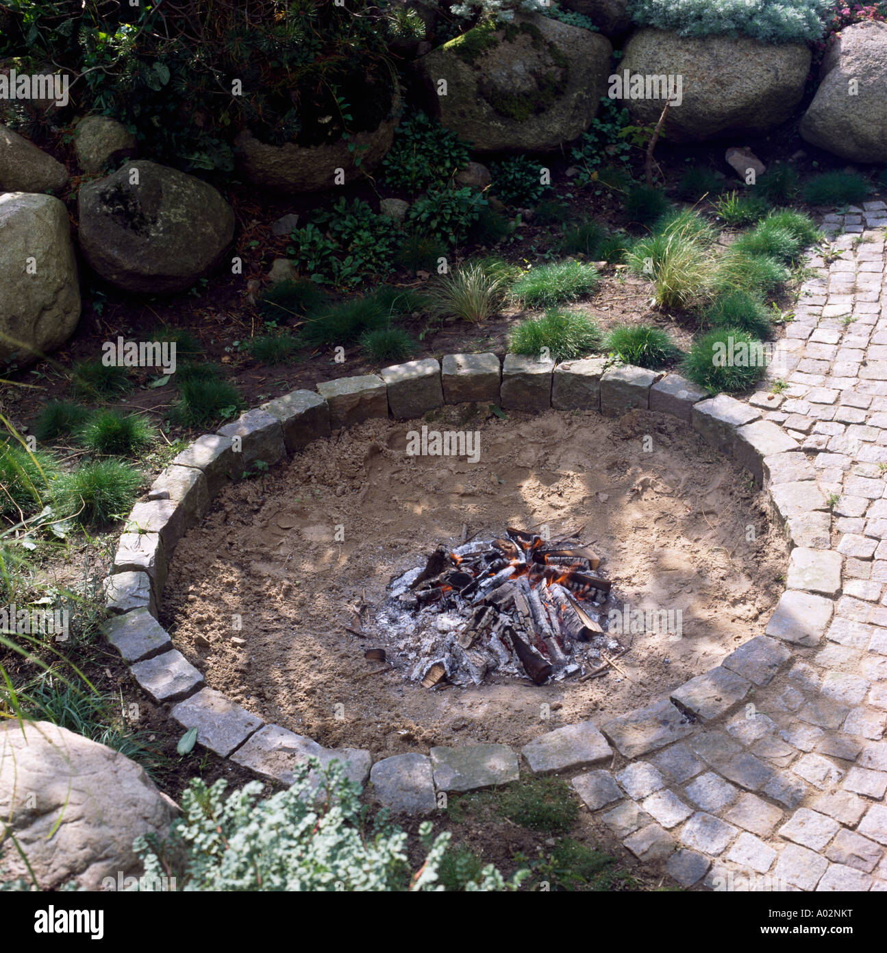 Paved-edge circular sandpit with log fire Stock Photo - Alamy