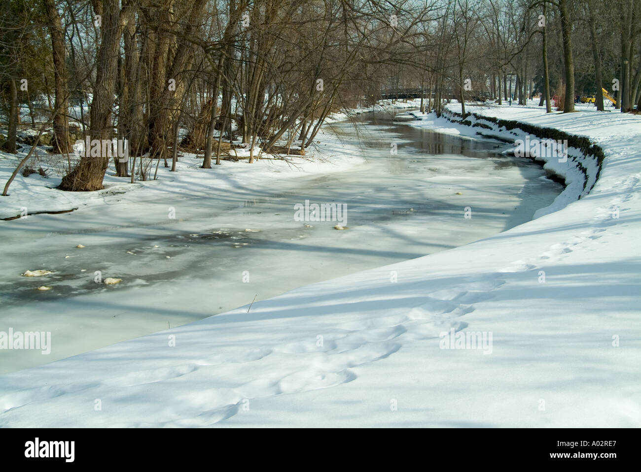 A winding s curved half frozen river creek flowing under a bridge Stock ...