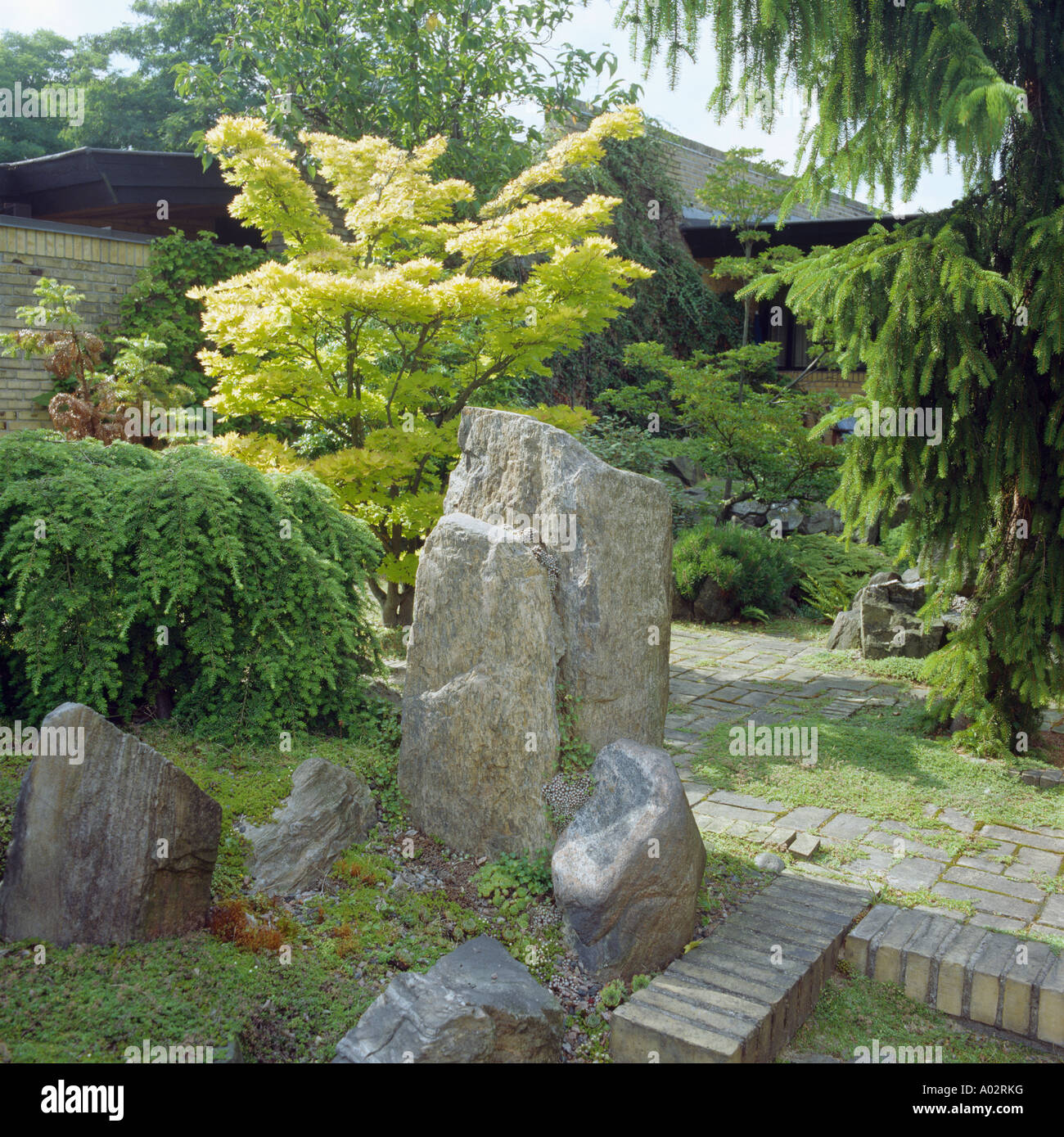 Rocky monolith sculpture on paving with small tree in background in ...