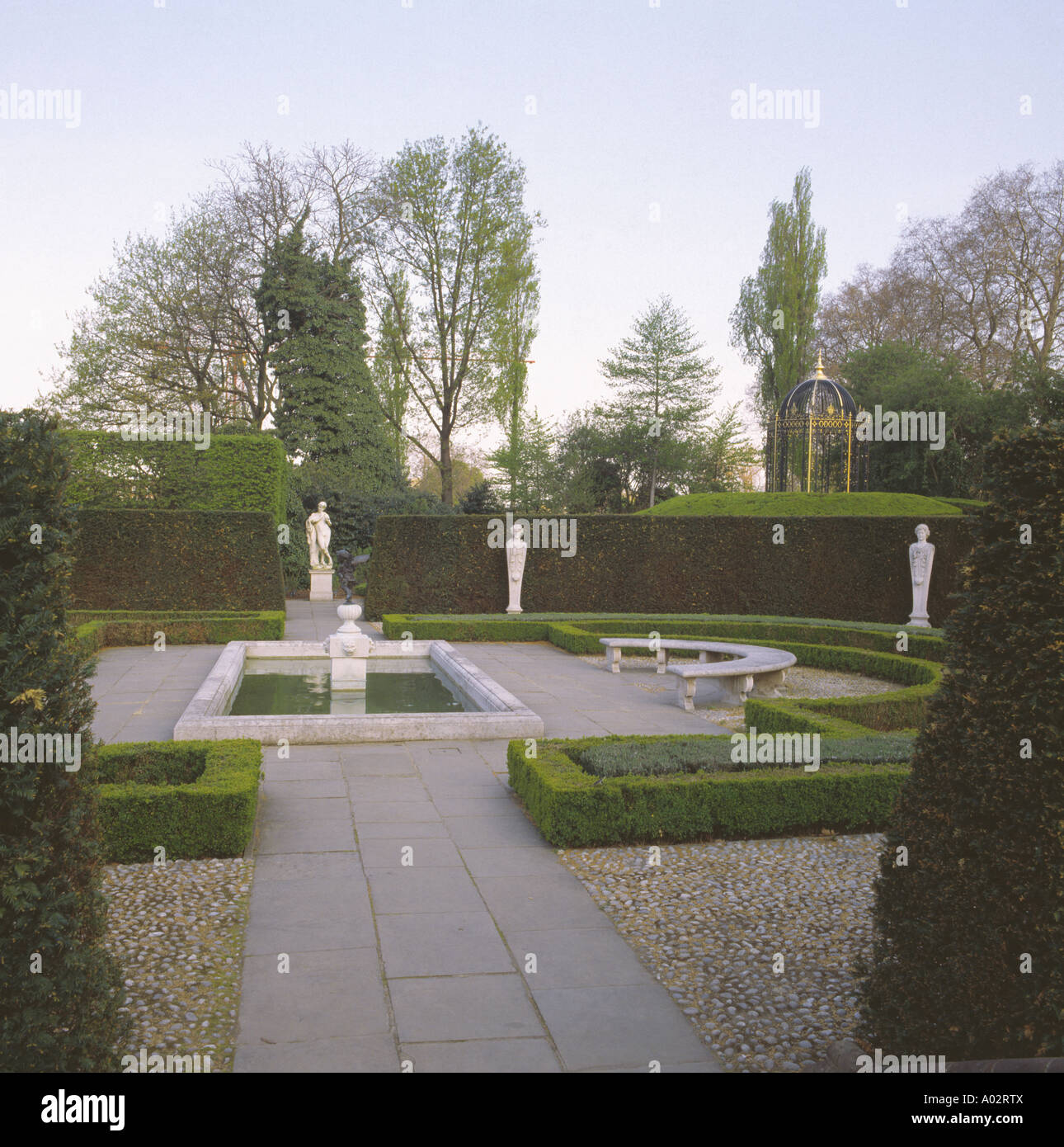 Formal garden bordered with clipped hedge with paving and statuary ...