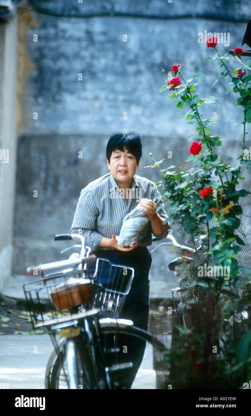 Chinese woman with her bicycle in the back streets of Beijing old city ...