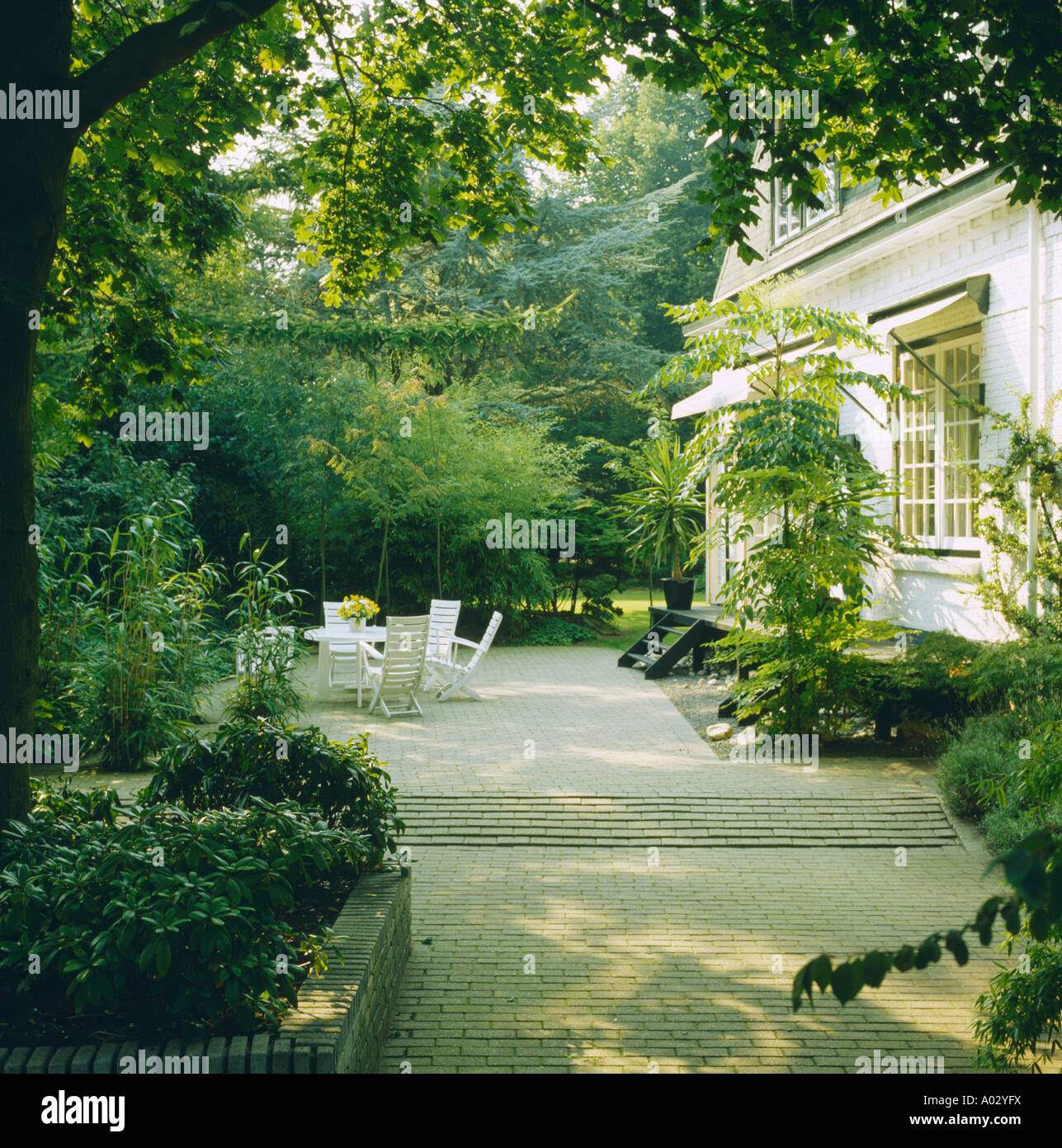 Paved shady terrace with furniture in front of white country house ...