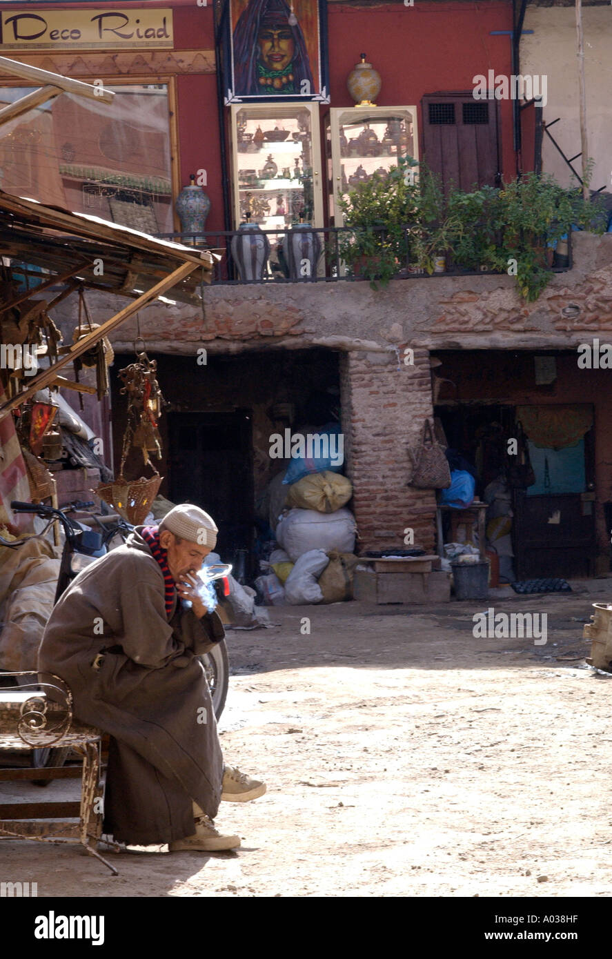 A Moroccan man in tradional clothing relaxes and has a smoke away from ...