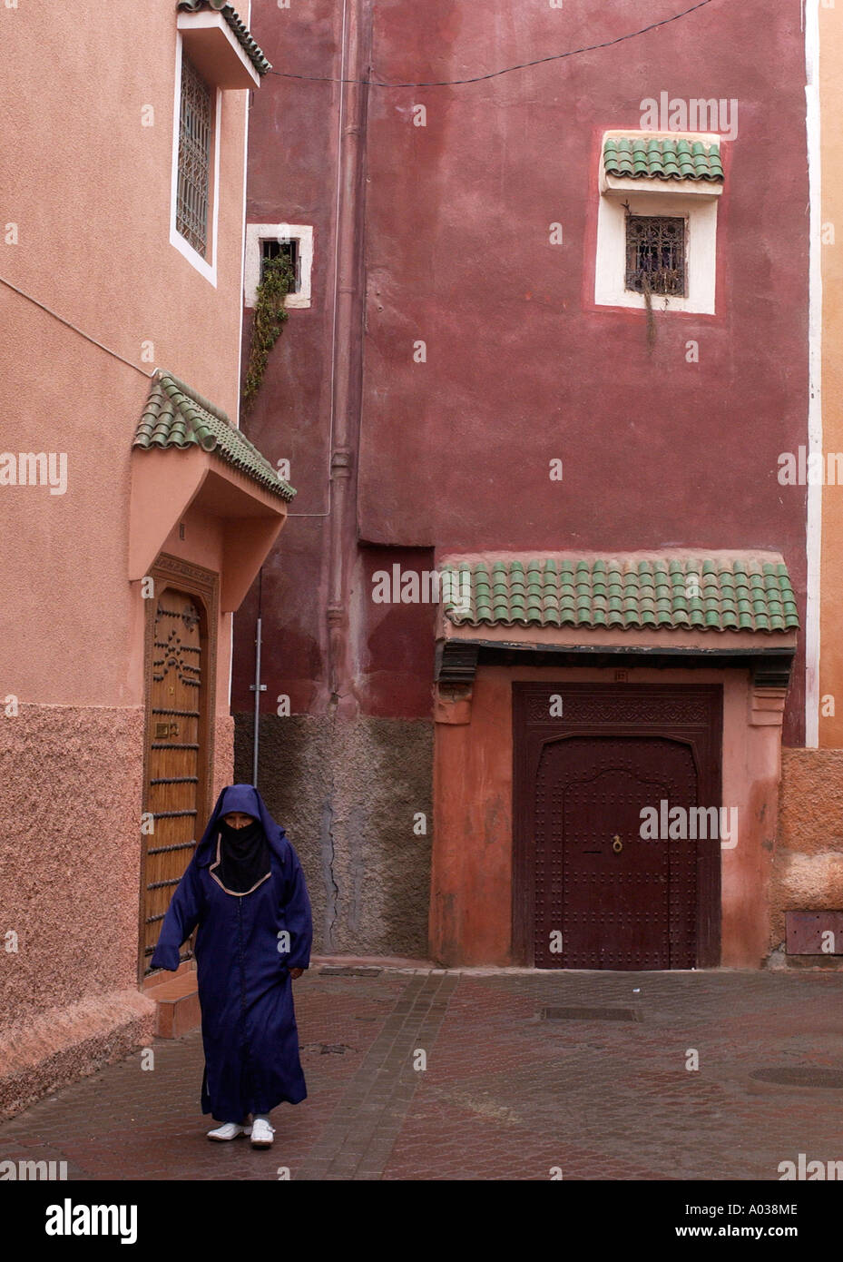 A Moroccan woman in traditional clothing walks through a back street of ...