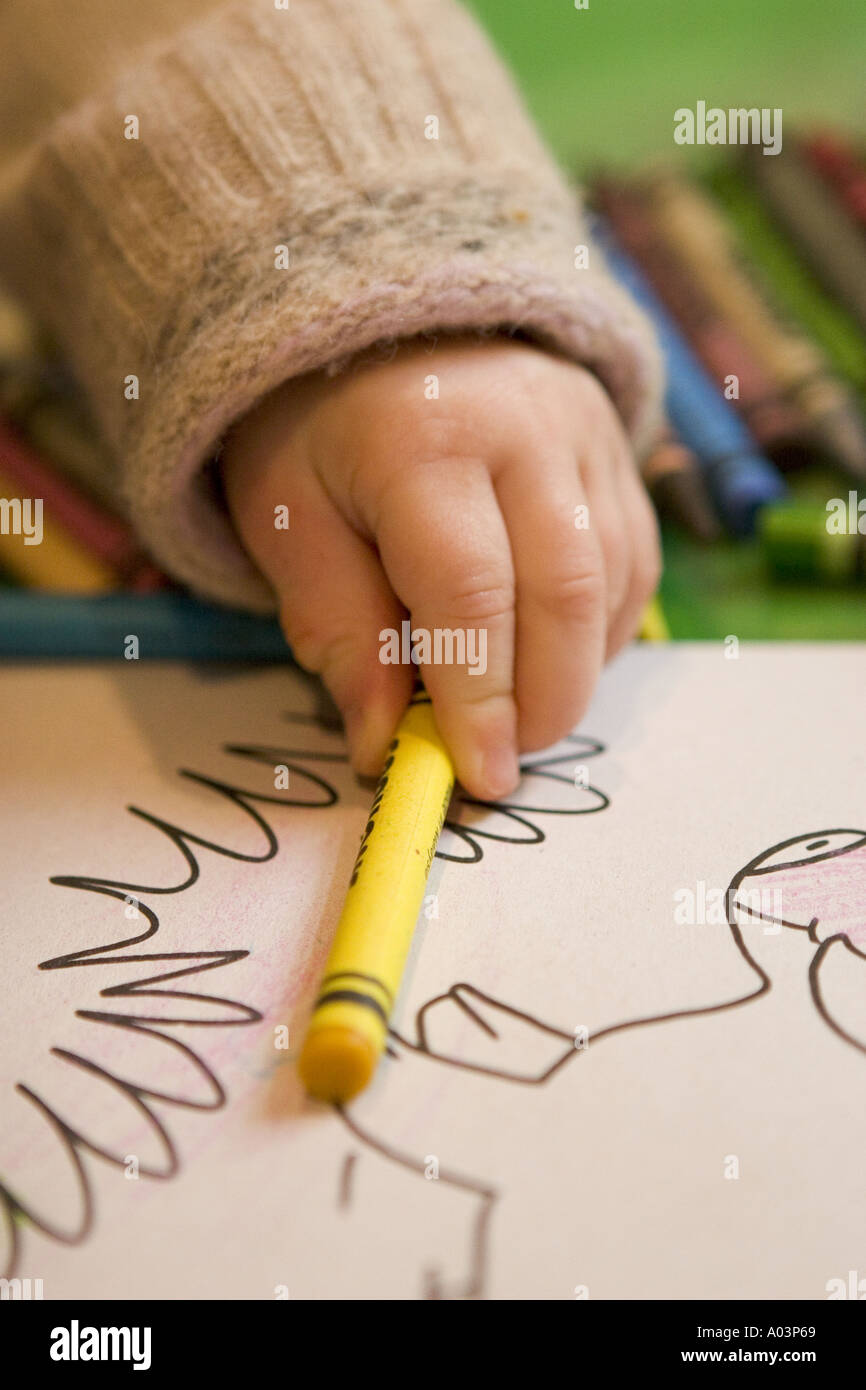 The hand of a child aged 1 to 2 years picking up a yellow wax crayon ...