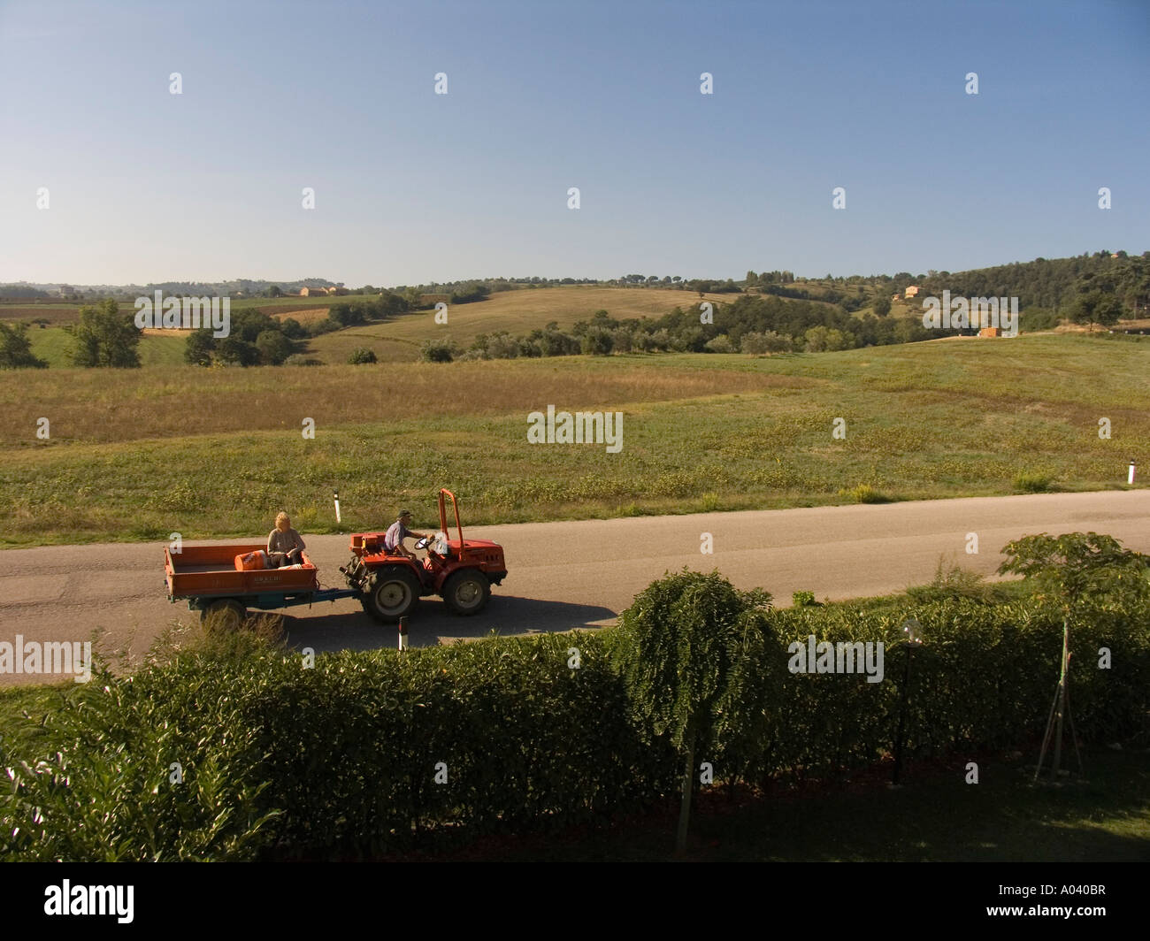 Italian farmer drives tractor with his wife riding in trailer up road ...