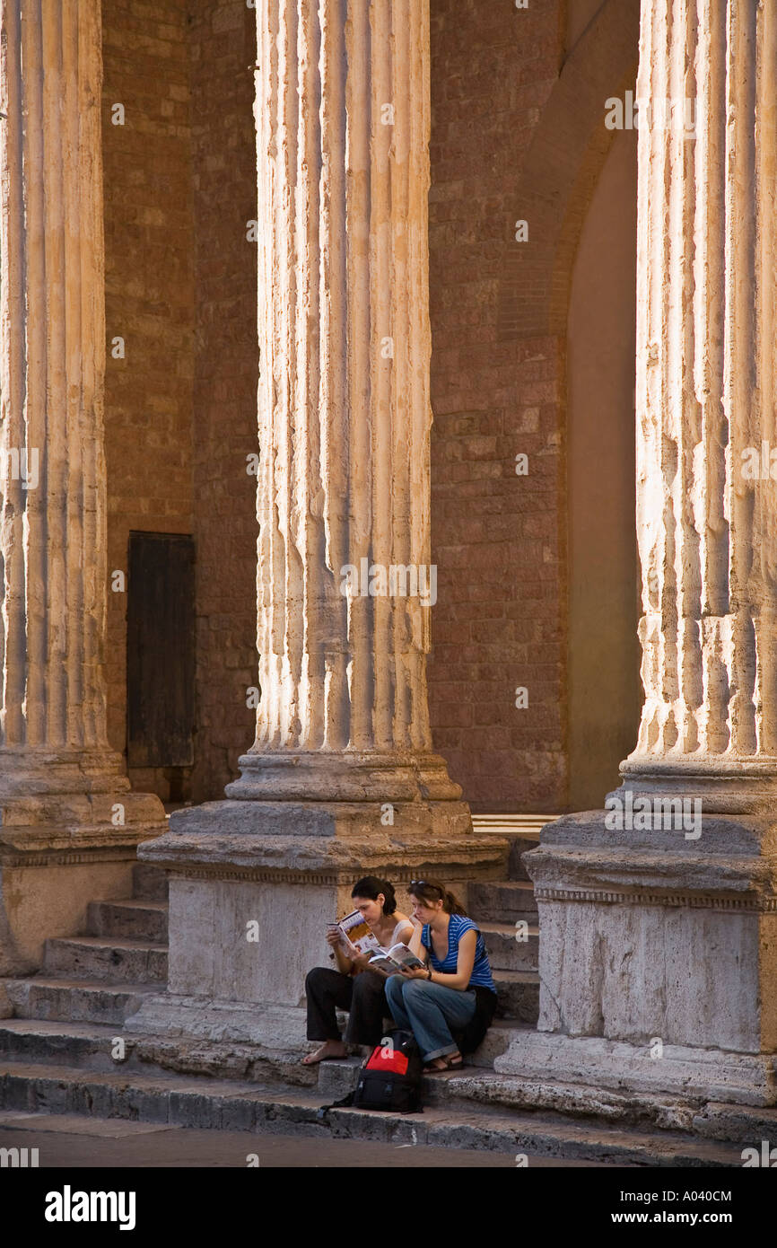 Two women sit on steps of the Roman temple Tempio di Minerva studying ...
