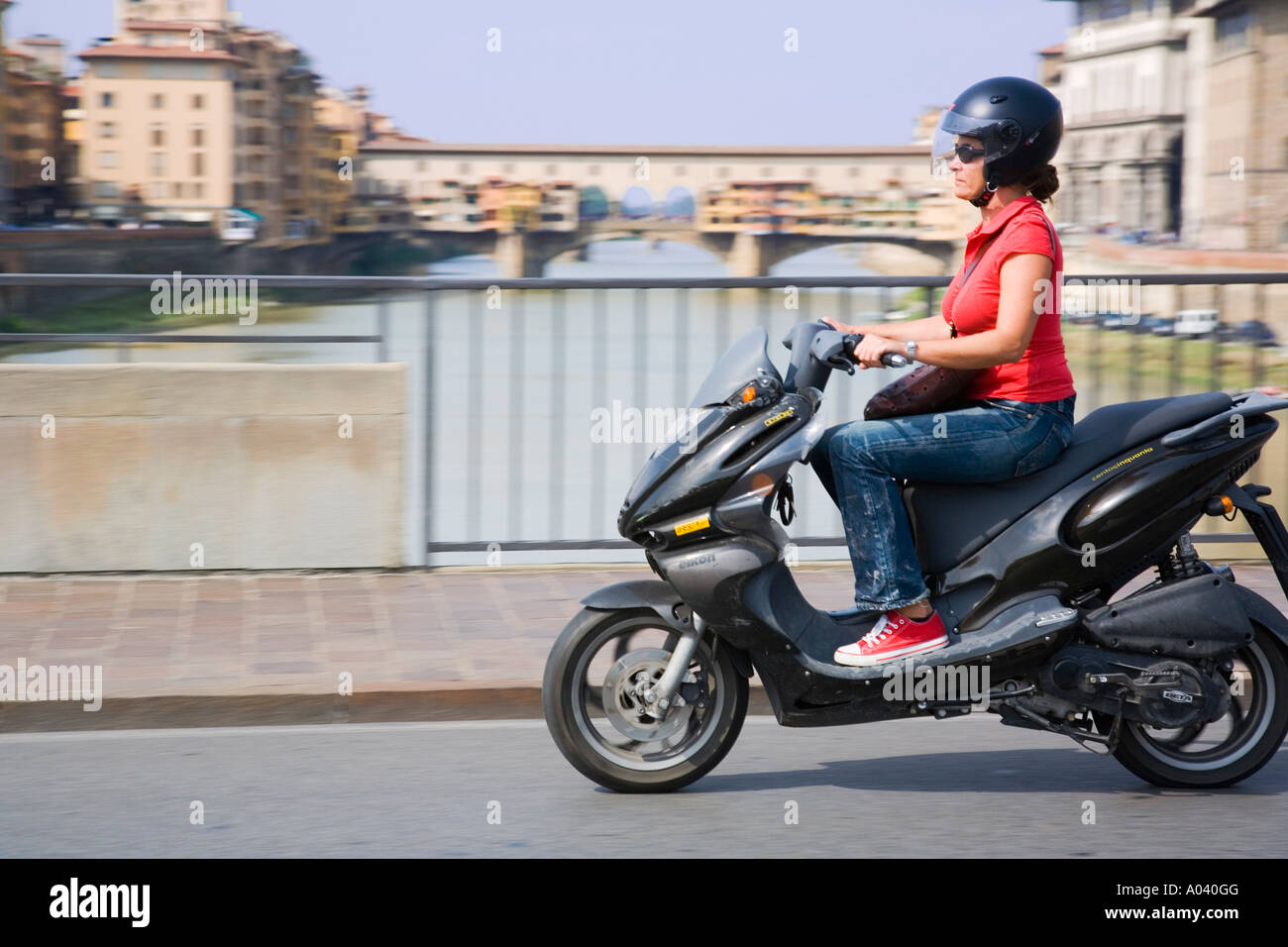 Woman riding scooter across Ponte allle Grazie with Ponte Vecchio in ...