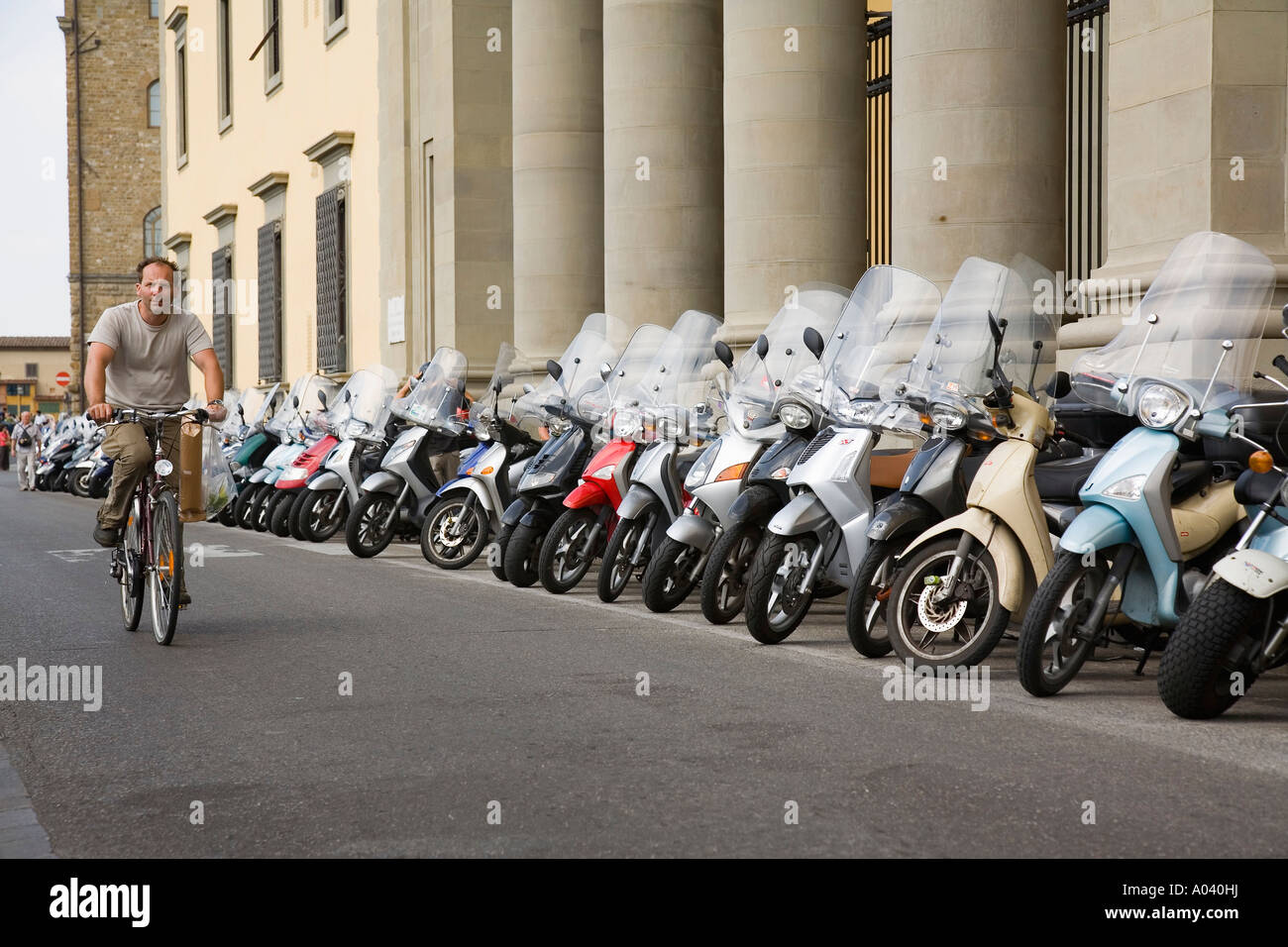 Man riding bicycle past line of scooters parked on street near Ponte ...