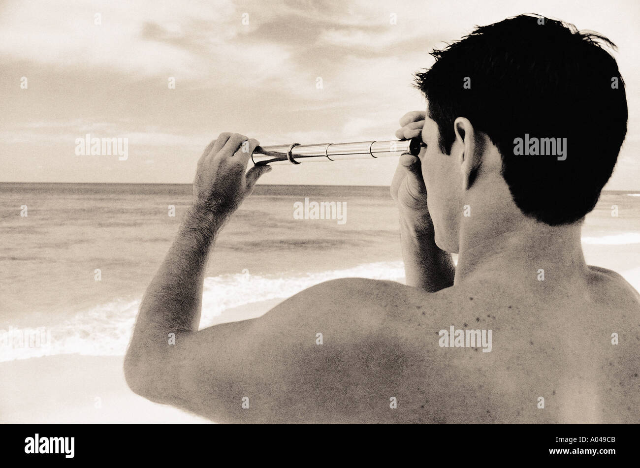 Young man standing on the beach looking out to sea with a telescope ...