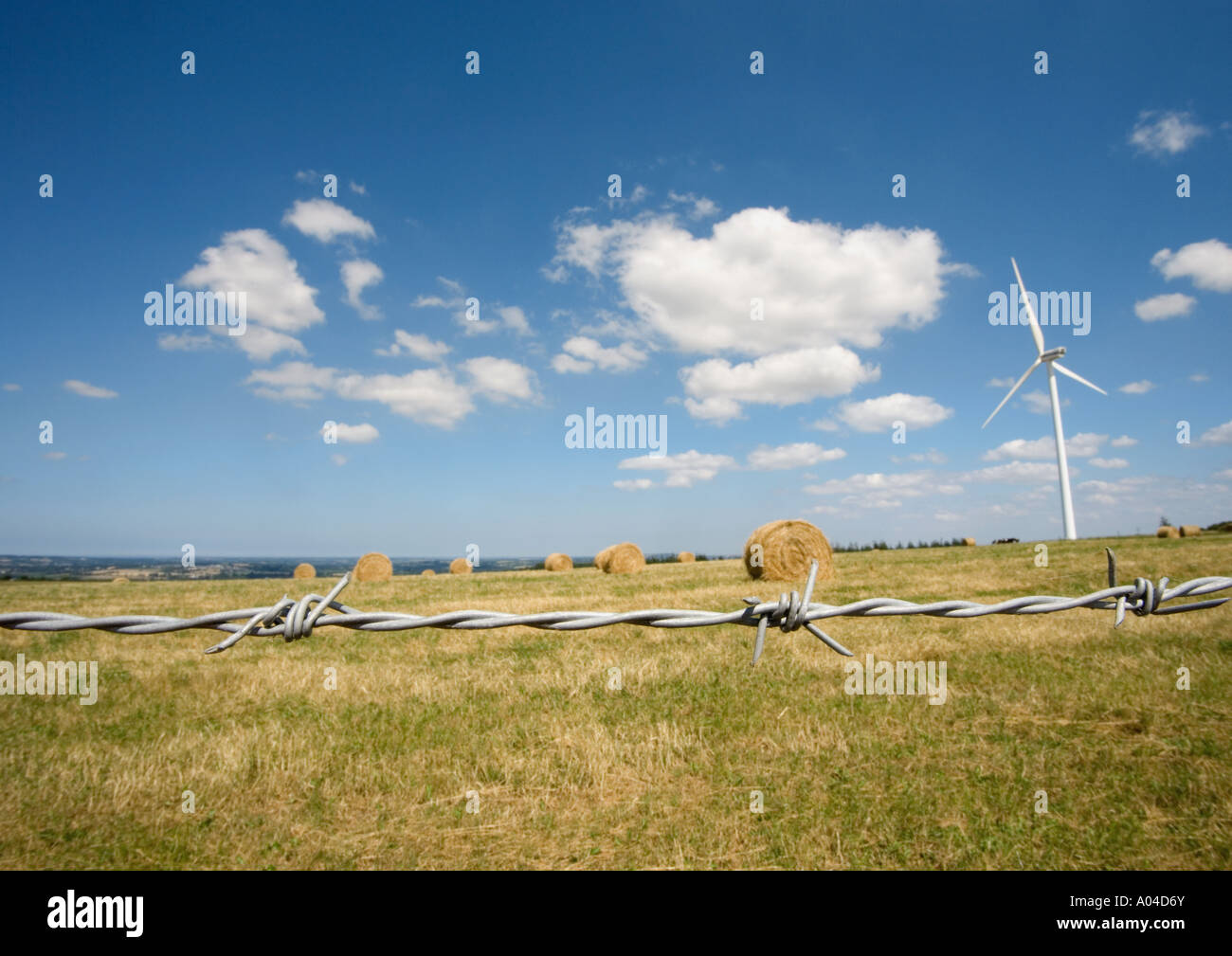 Wind turbine in field with bales of hay, barbed wire in foreground ...